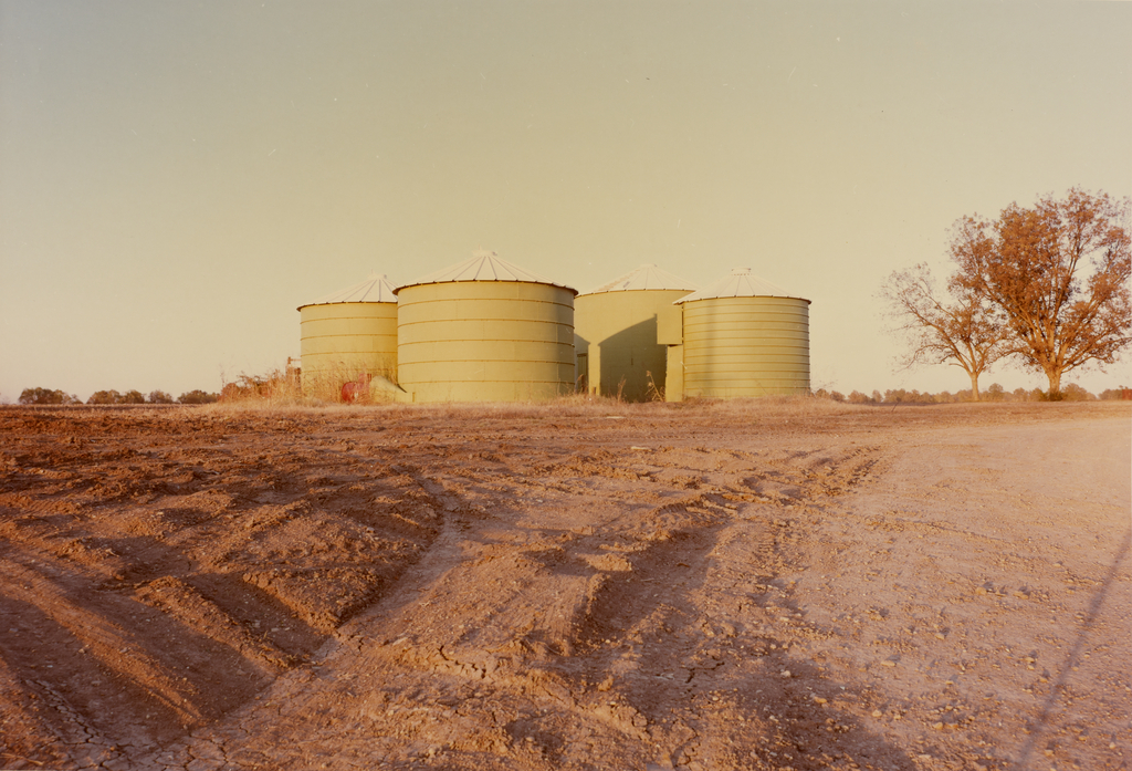 [Rutted field with four grain silos in background] (Getty Museum)